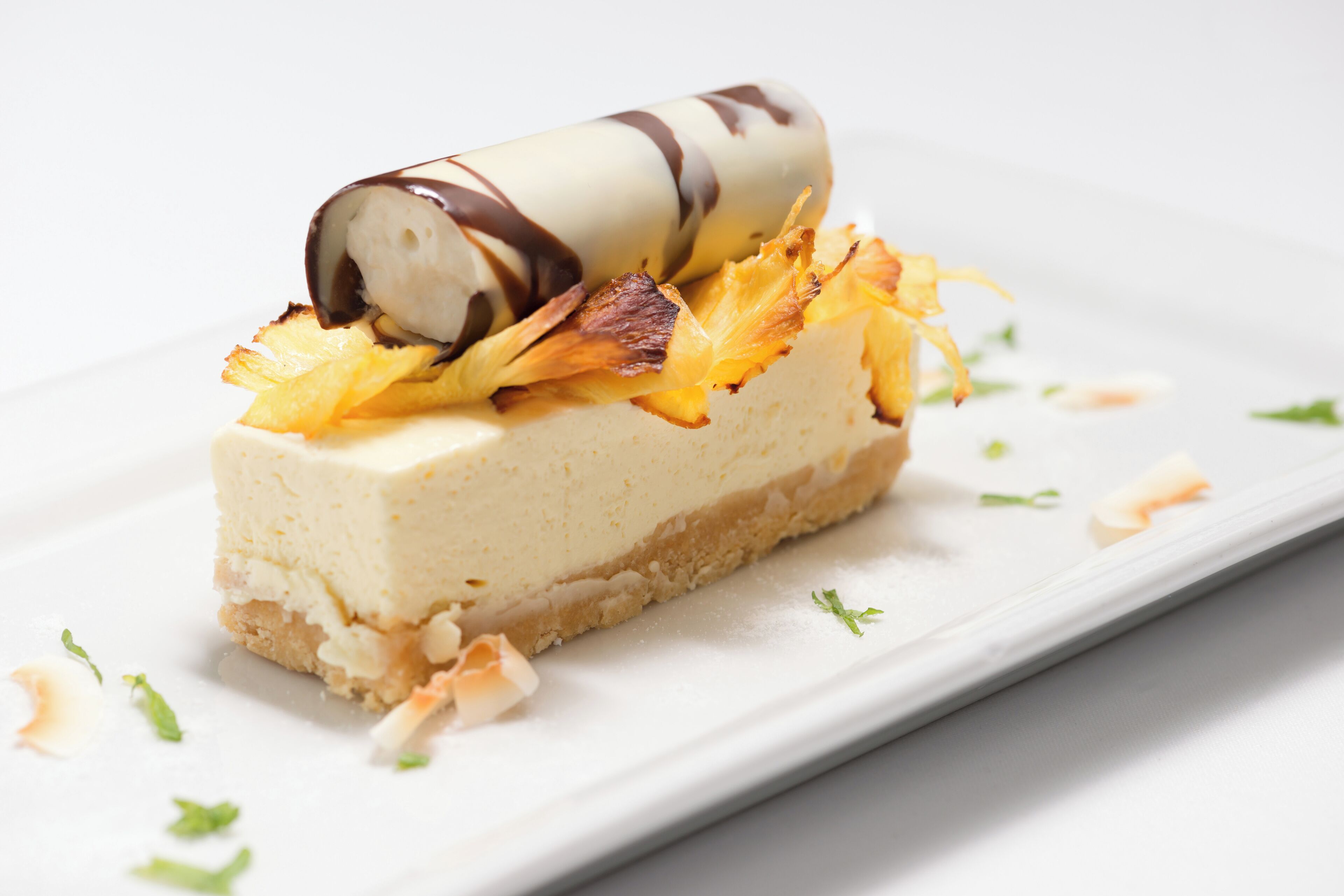 Uma fatia de cheesecake com calda de chocolate e guarnição de abacaxi sobre um prato branco.