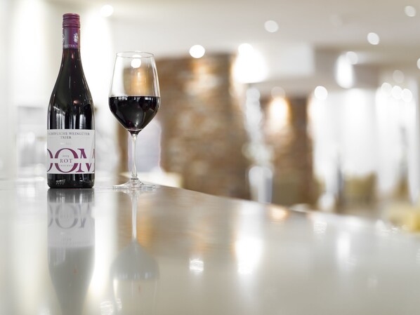 Uma garrafa de vinho e um copo sobre uma superfície refletora.
