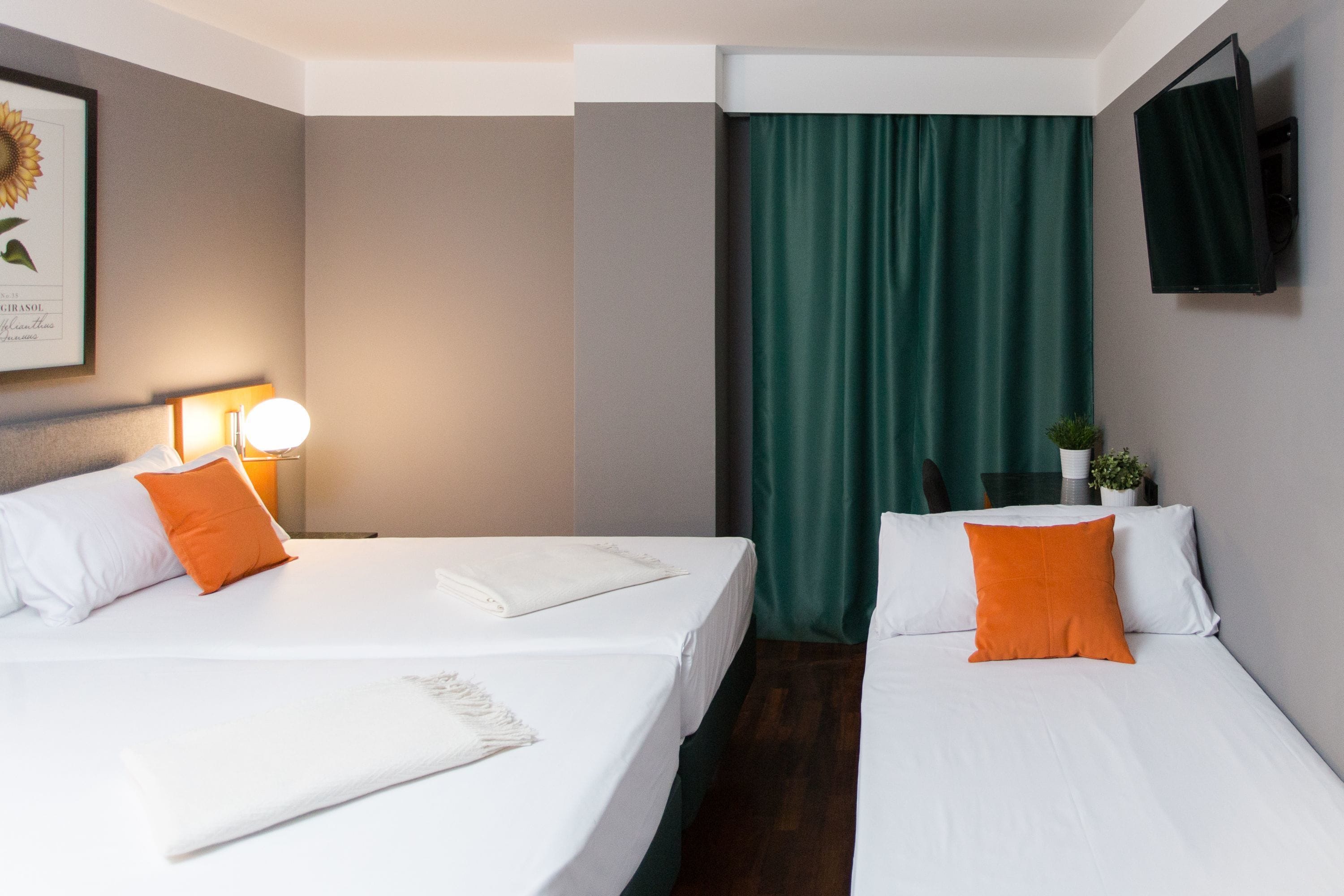 Quarto de hotel com duas camas, uma escrivaninha, uma cadeira, uma televisão e uma janela com cortinas.