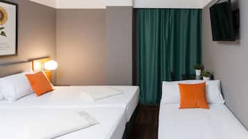 Quarto de hotel com duas camas, uma escrivaninha, uma cadeira, uma televisão e uma janela com cortinas.
