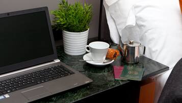 Um laptop sobre uma mesa de mármore, uma chávena branca, uma planta verde, um jarro de café prateado, um livro e uma toalha branca.