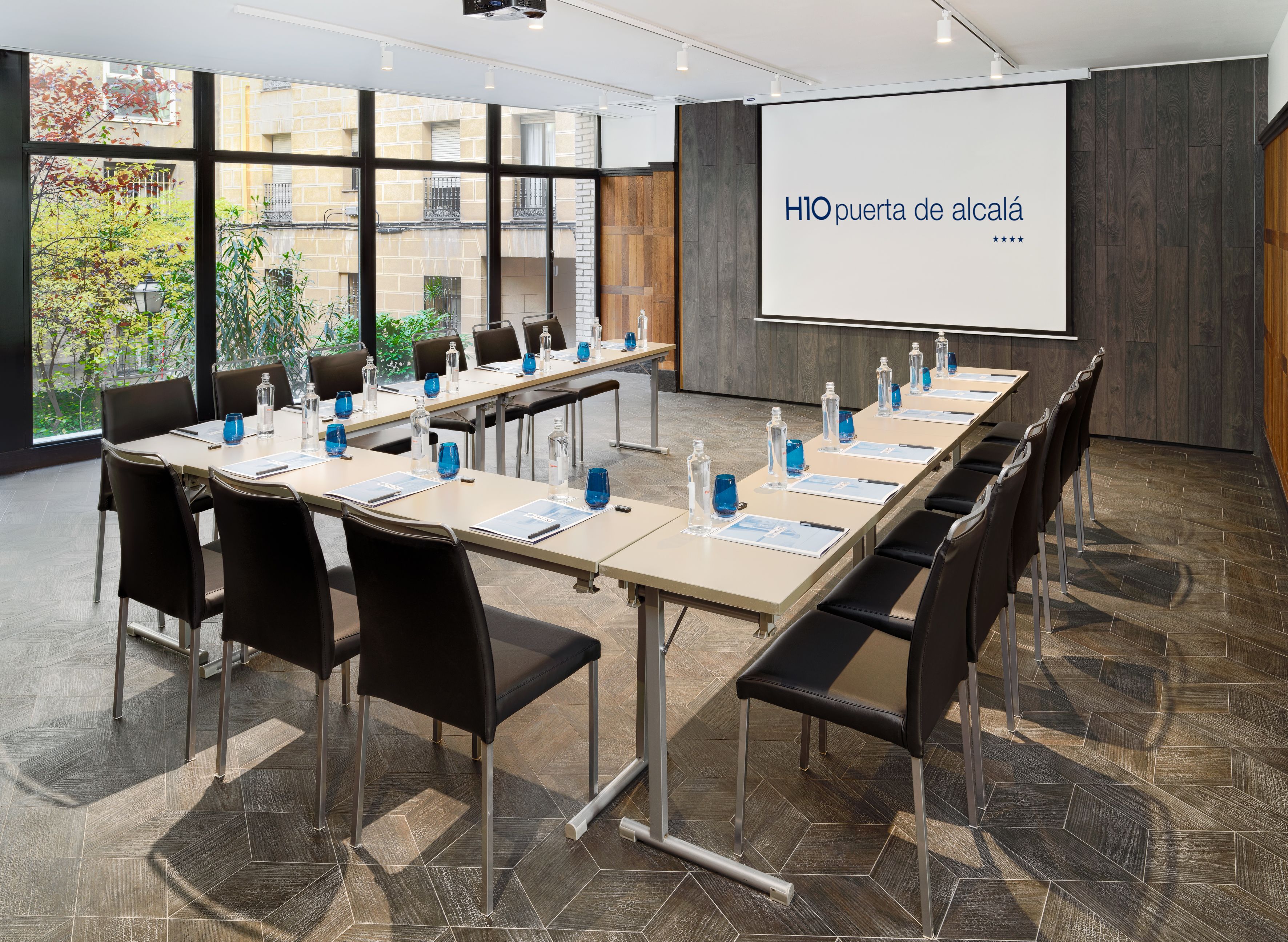Sala de conferências com uma mesa comprida, cadeiras e tela de projetor exibindo texto.