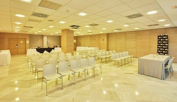 Uma sala de conferências com fileiras de cadeiras, um palco com um púlpito e um banner na parede.