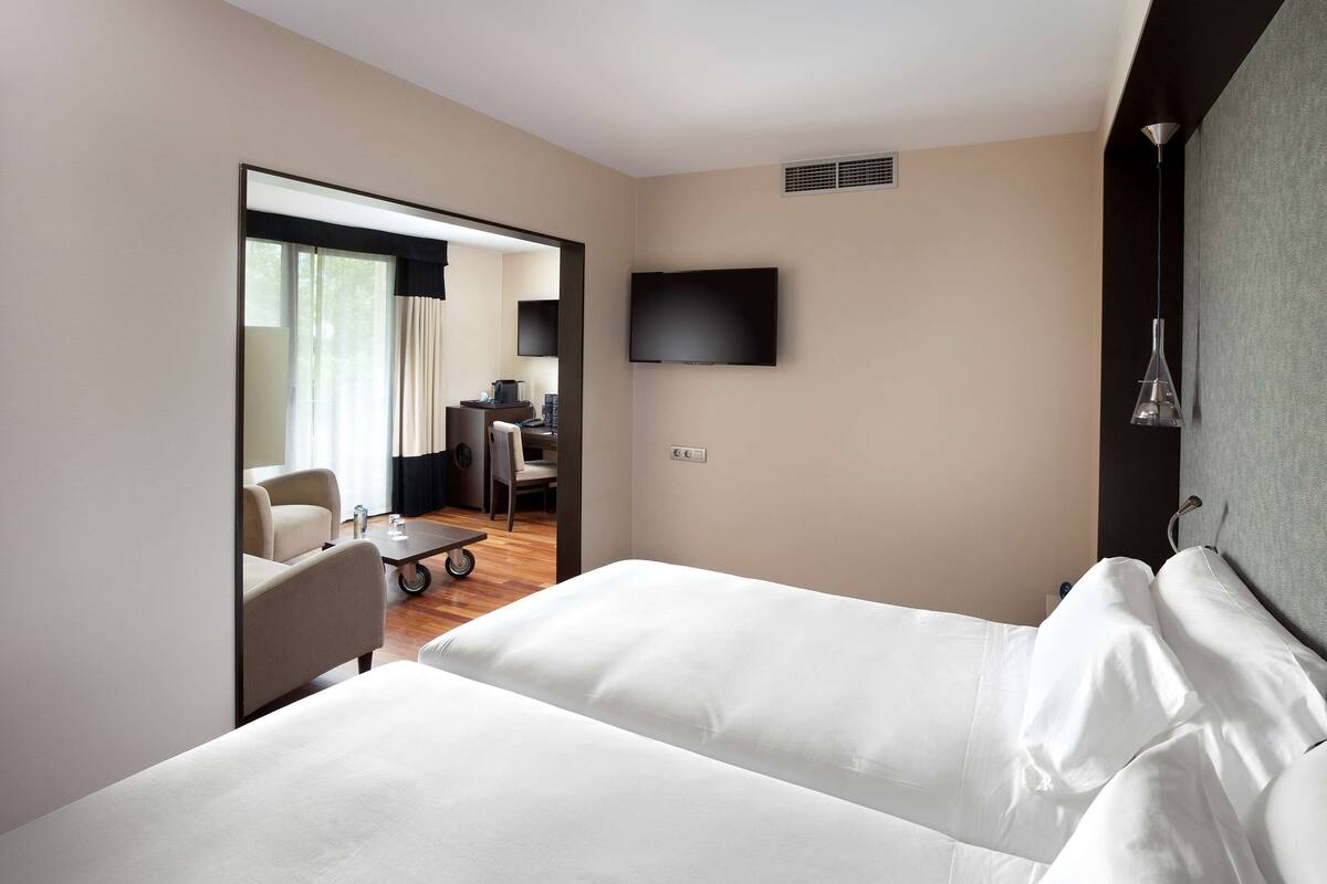 Quarto de hotel com duas camas, uma escrivaninha, uma cadeira, televisão e vista para o exterior.