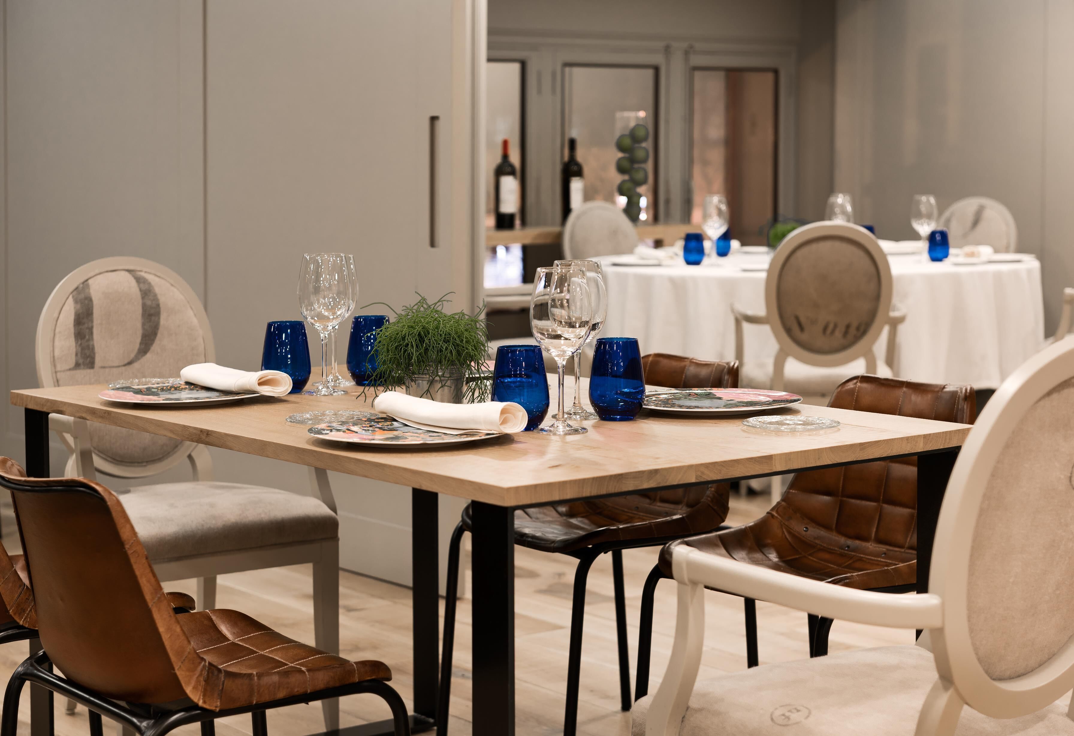 Uma sala de jantar com mesa de madeira posta para quatro pessoas, com copos azuis e pratos brancos.