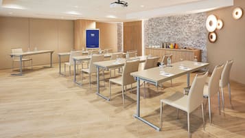 Uma sala de conferências moderna com várias mesas e cadeiras, uma tela de projetor e uma parede decorativa com luminárias circulares.