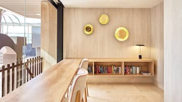 Interior moderno com mesa de madeira, cadeiras, estante e luminárias decorativas na parede.