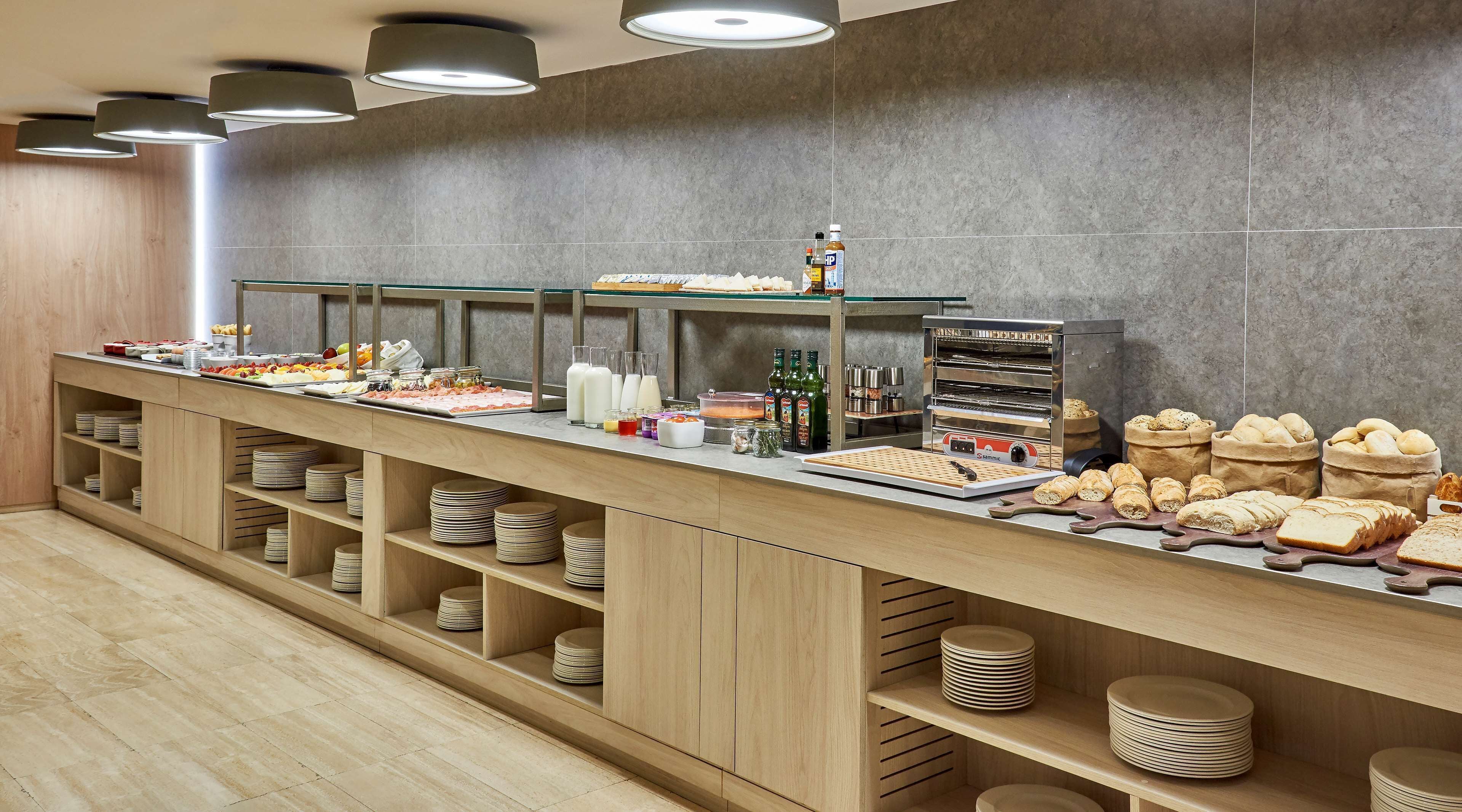 Disposição de buffet com diversos alimentos, bebidas e um forno para pão.