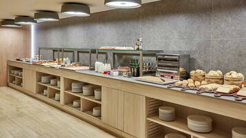 Disposição de buffet com diversos alimentos, bebidas e um forno para pão.