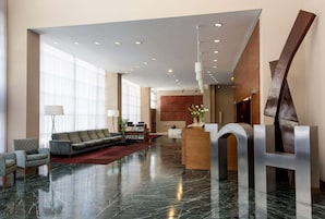 Um hall amplo com uma recepção moderna, área de estar com sof ás e uma grande escultura em formato de H.