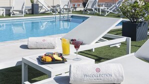 Uma área de descanso à beira da piscina com uma mesa posta para refeição, bebida e uma toalha com logotipo.