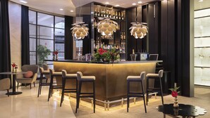 Uma área de bar moderna com balcão central, vários bancos e um lustre decorativo.