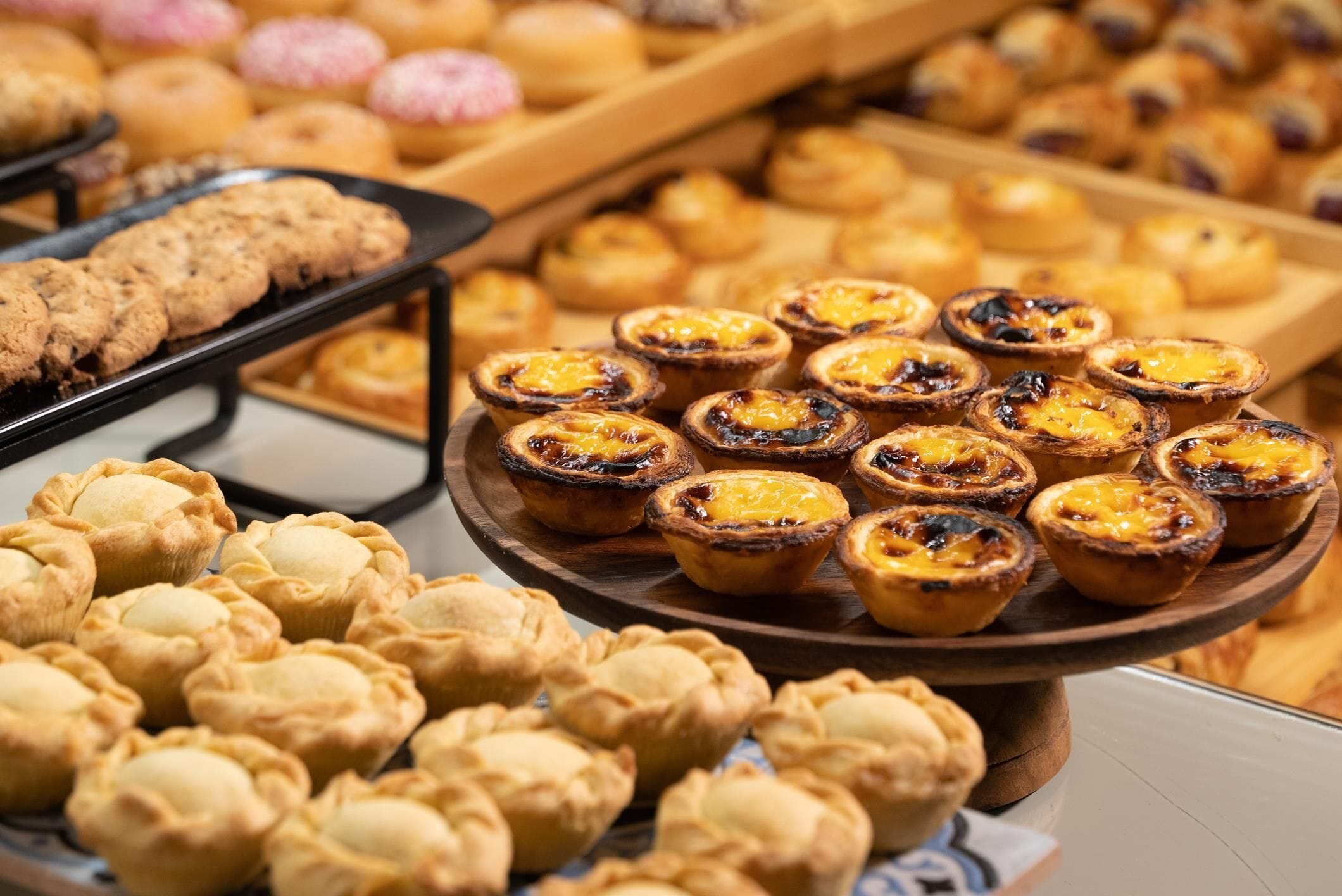 Diversos produtos de panificação, incluindo biscoitos, tortas e doces, dispostos em bandejas.