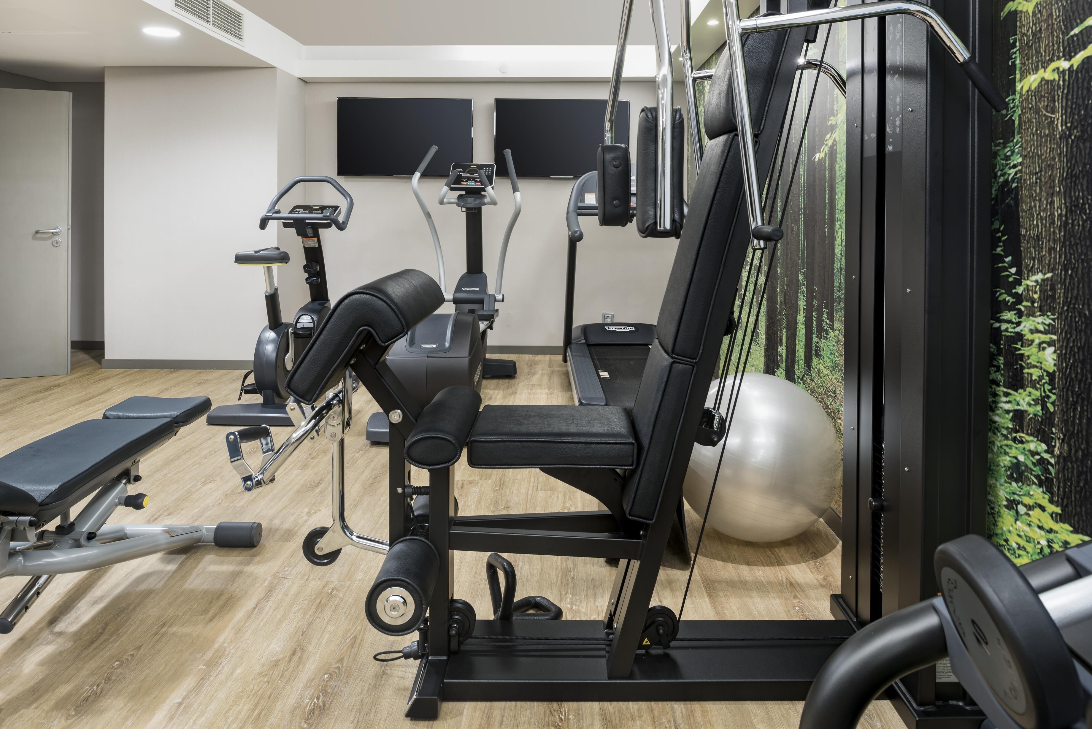 Uma academia com diversos equipamentos de exercícios, incluindo um banco, elíptico e aparelho de musculação.