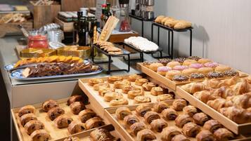 Diversos pastéis e produtos de panificação expostos em travessas e mesas de madeira, com molhos e bebidas ao fundo.