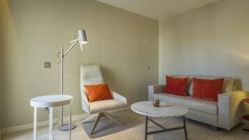 Uma sala de estar moderna com um sofá branco, almofadas laranja, uma mesa de centro redonda, um abajur de chão e um abajur de mesa.