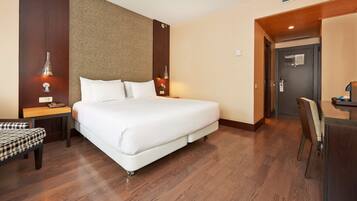 Quarto de hotel com uma cama grande, mesas de cabeceira, escrivaninha e uma cadeira.