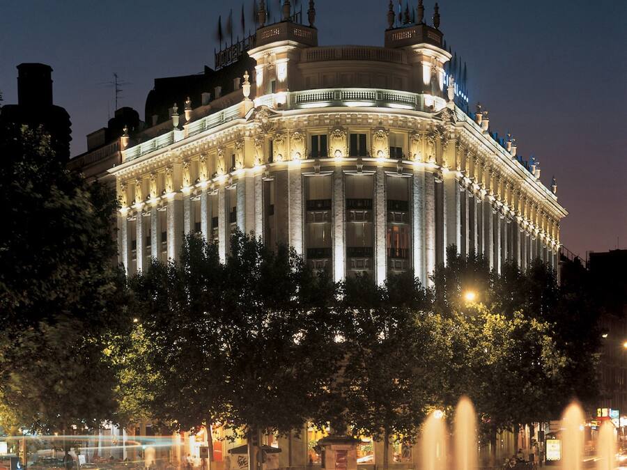 Um edifício imponente e iluminado, com arquitetura clássica, caracterizado por colunas altas e detalhes ornamentados.