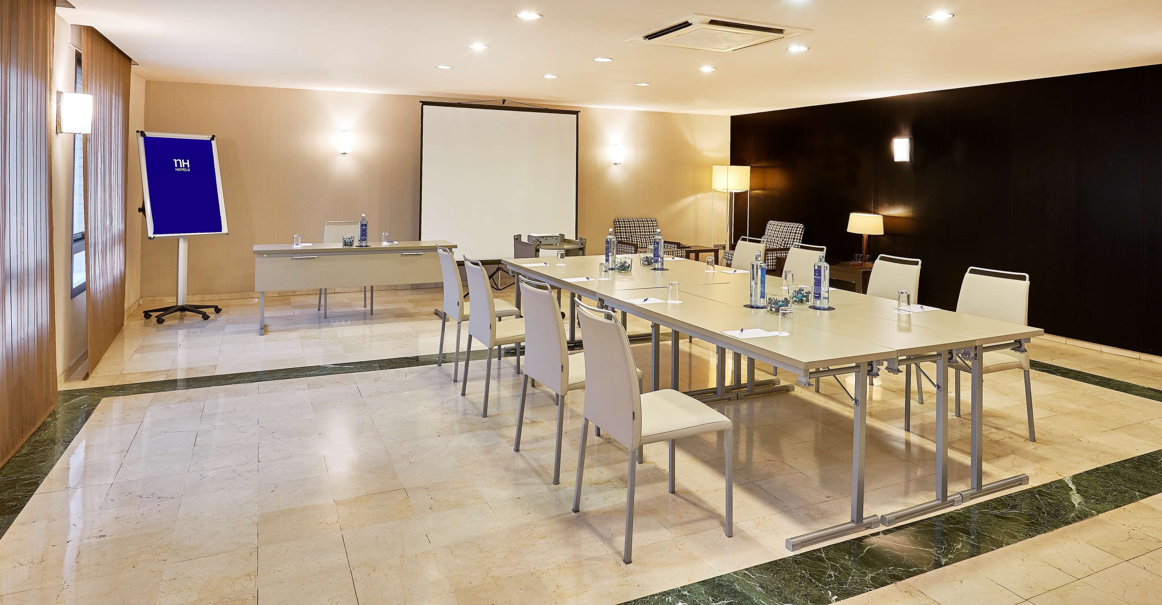 Uma sala de conferência com uma mesa comprida, cadeiras, uma tela de projetor e um quadro branco.