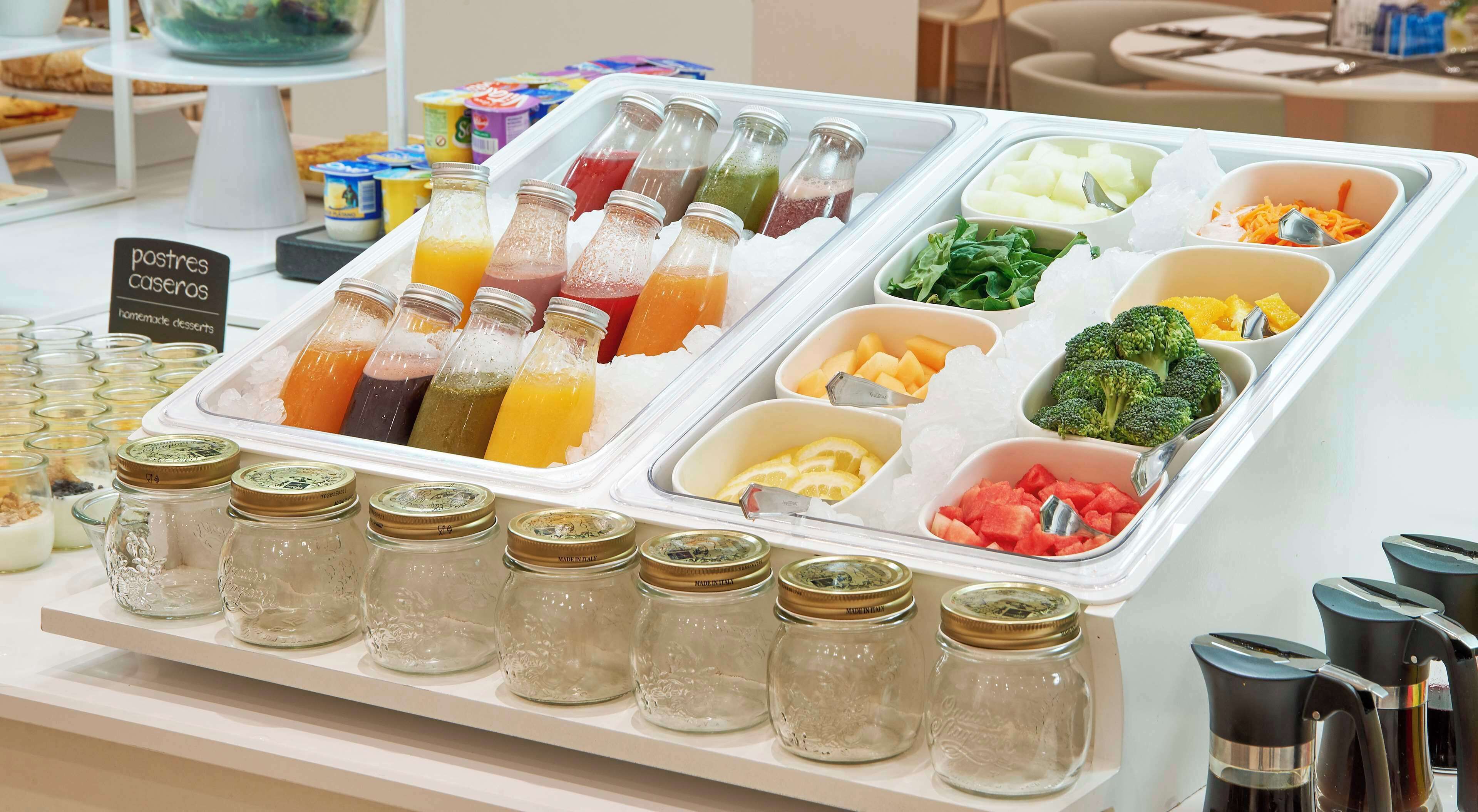 Um buffet de café da manhã com diversas opções de comida e bebida, incluindo sucos, iogurte e frutas frescas.