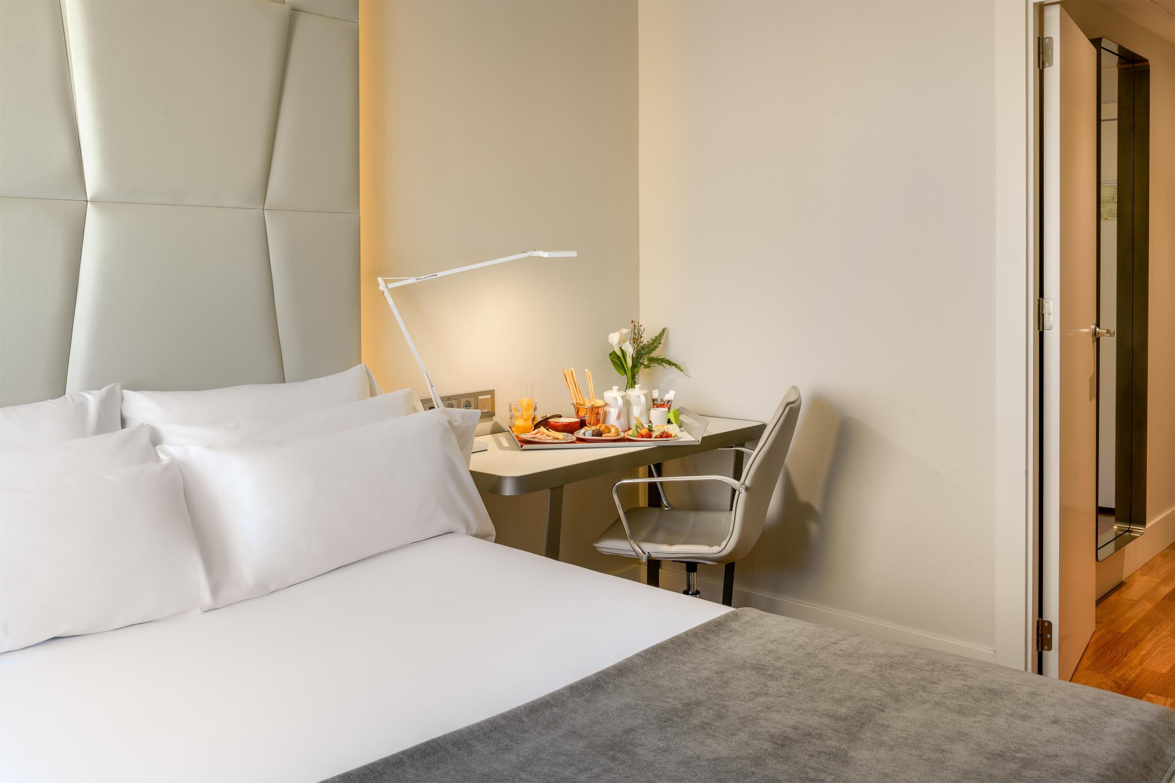 Quarto de hotel moderno com cama, mesa de trabalho com café da manhã e uma cadeira.