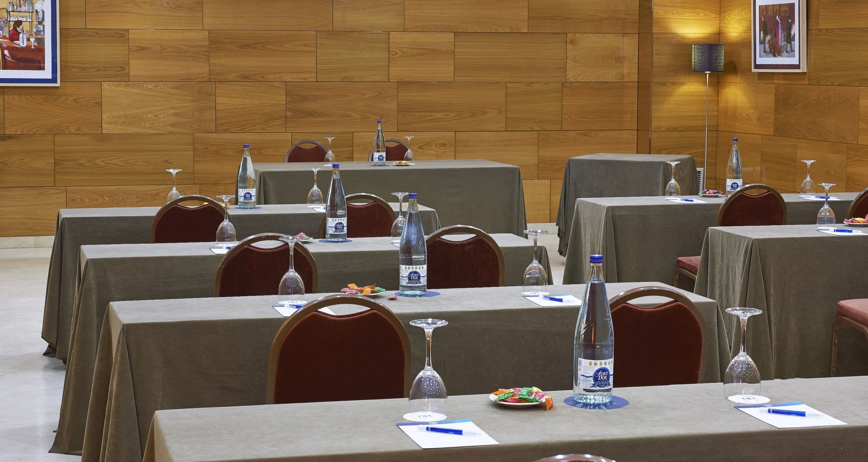 Sala de conferências com várias mesas, cada uma com garrafas de água, copos de vinho e placas de identificação.