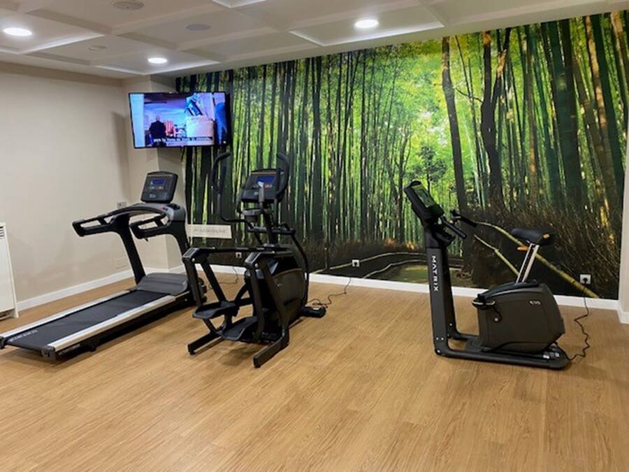 Uma academia com três esteiras, uma bicicleta ergométrica e uma tela de televisão na parede.