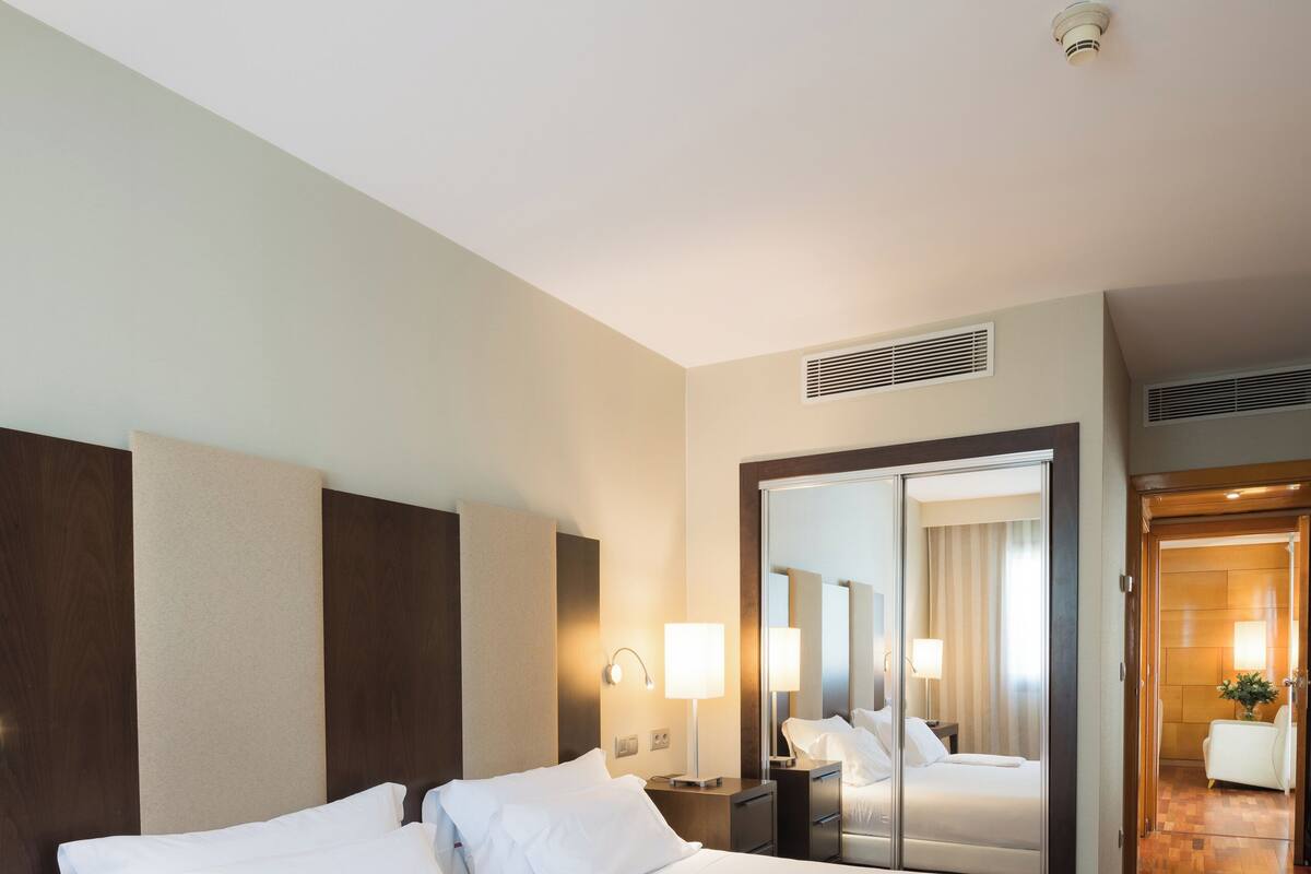 Quarto de hotel com uma cama grande, uma mesa de cabeceira, um espelho e uma porta para o banheiro.