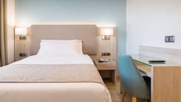 Quarto de hotel com cama, abajures, escrivaninha com cadeira e telefone.
