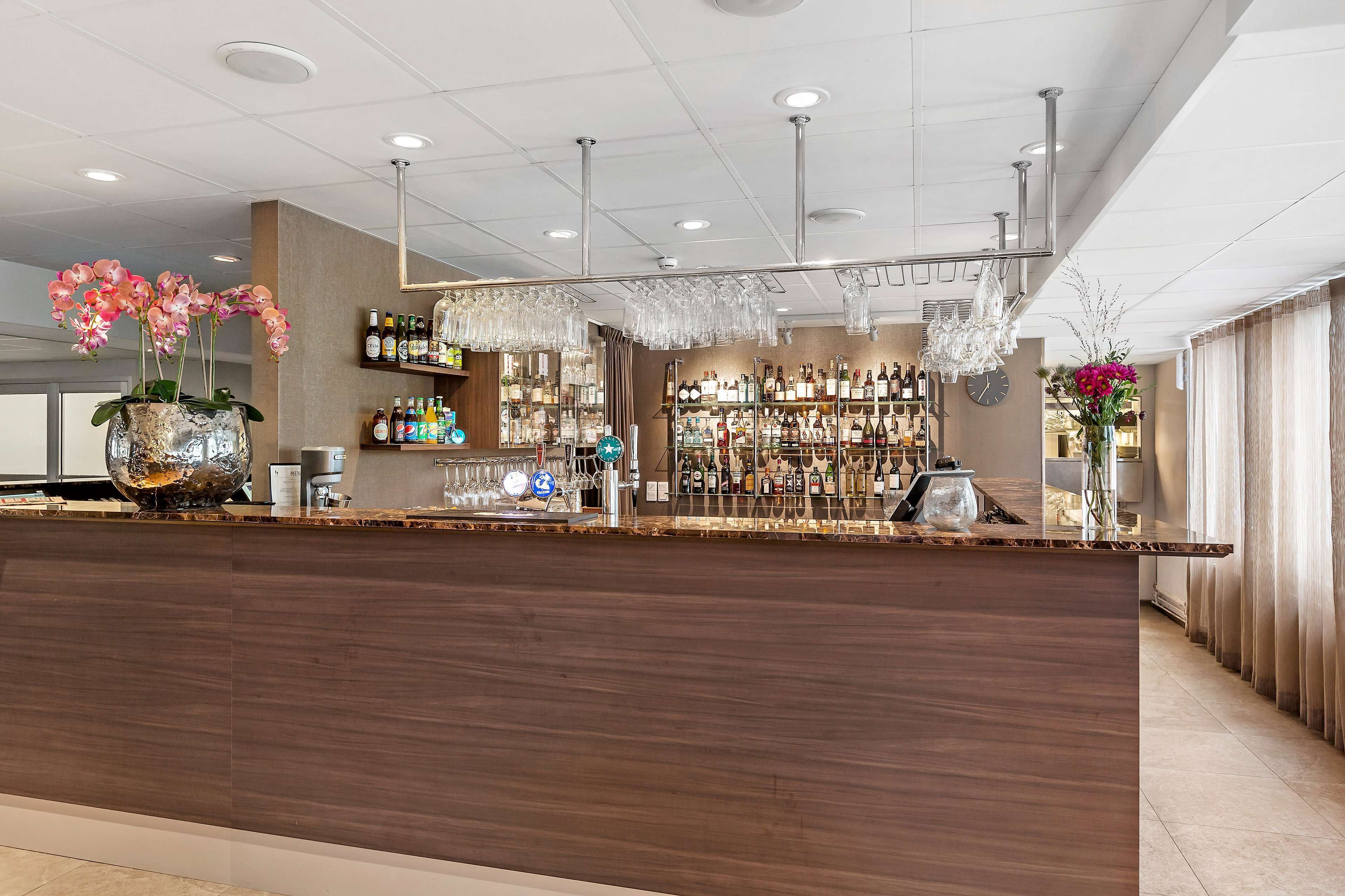 Uma área de bar com balcão de madeira, prateleiras com garrafas e lustres de cristal pendentes.