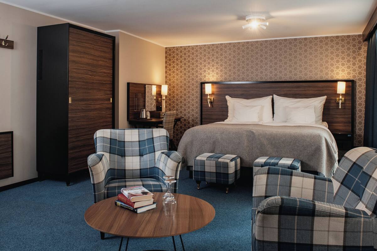 Quarto de hotel com uma cama, duas poltronas, uma mesa de centro, um criado-mudo e um guarda-roupa.