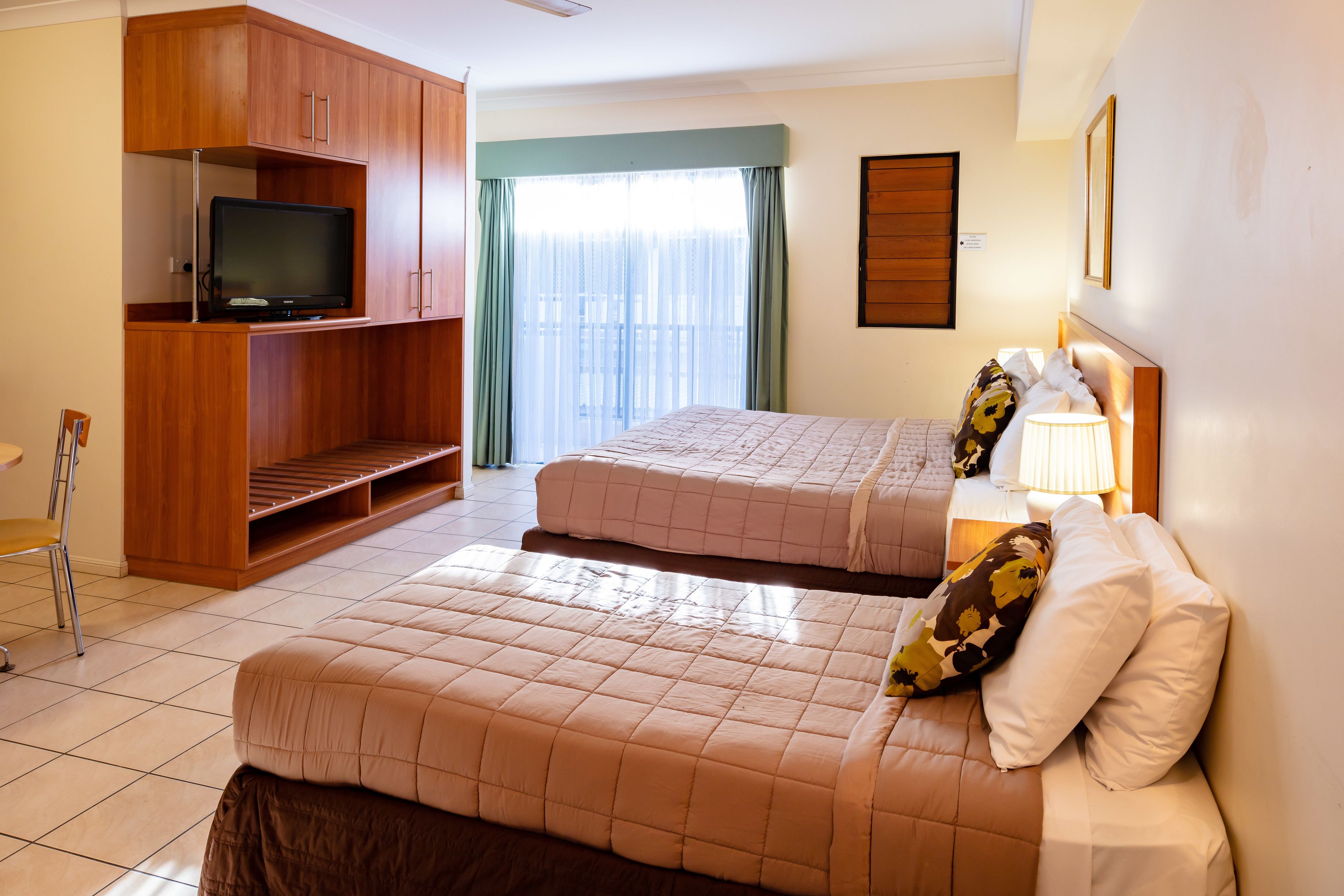 Quarto de hotel com uma cama, televisão, escrivaninha e janela com cortinas.