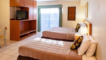 Quarto de hotel com uma cama, televisão, escrivaninha e janela com cortinas.
