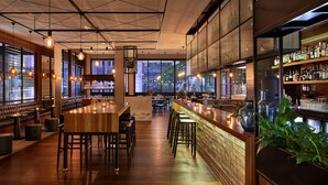 Uma área de bar moderna com um balcão de madeira comprido, assentos com bancos e luminárias pendentes.