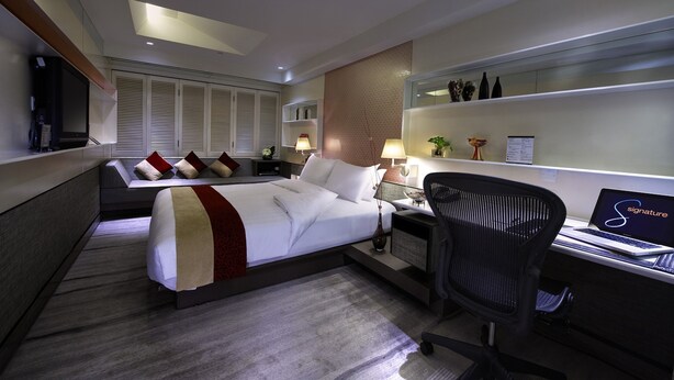 Quarto de hotel com cama, escrivaninha com laptop, cadeira, mesa de cabeceira e criado-mudo.