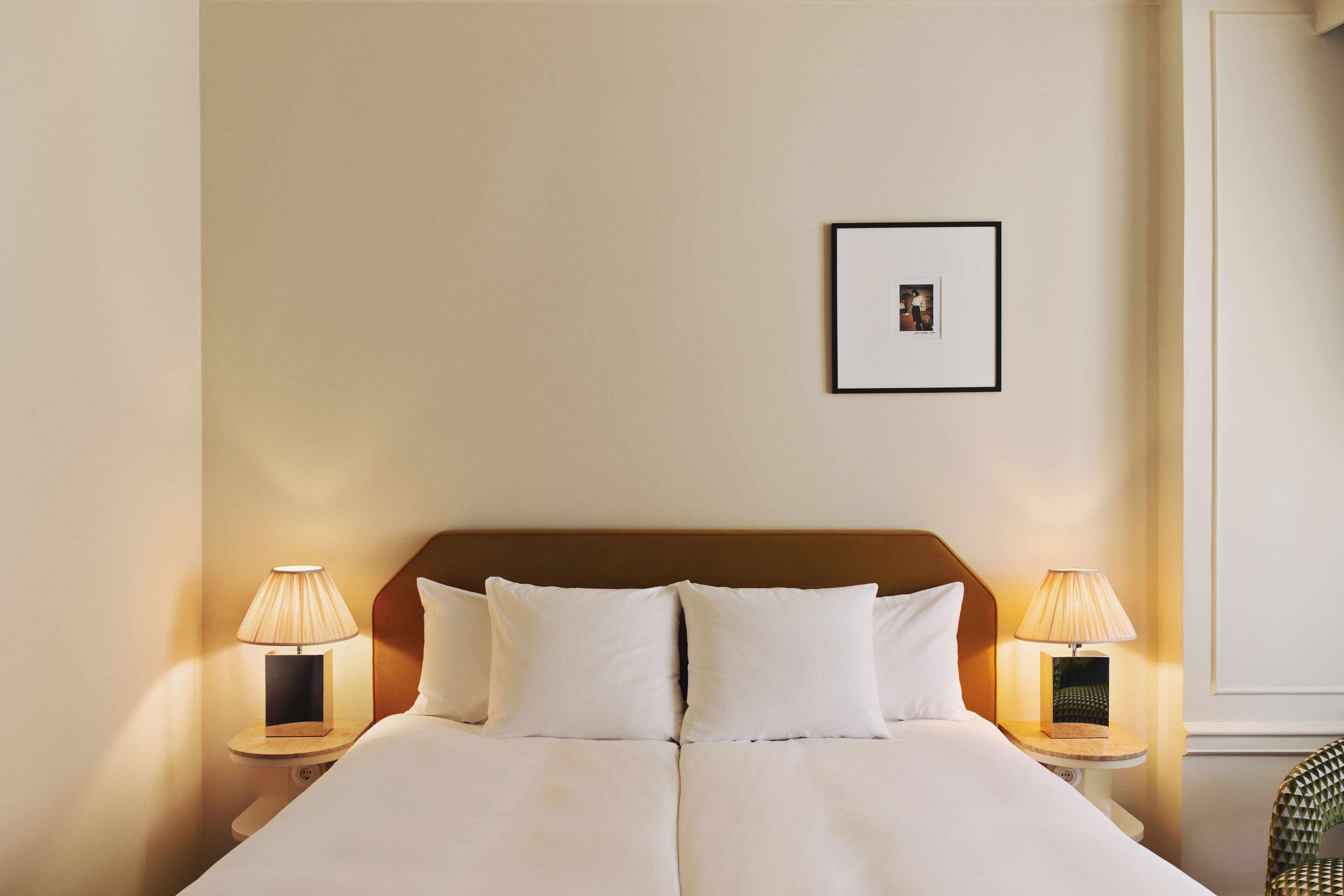 Cama bem arrumada com lençóis brancos, duas luminárias de cabeceira e um quadro na parede.