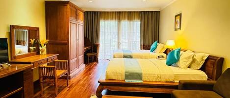 Quarto de hotel com cama, escrivaninha, cadeira, mesa de centro com frutas e televisão.
