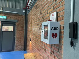 Um edifício de tijolos com uma porta identificada como 'LUGAR', uma caixa de DEA e um telefone.
