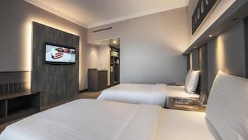 Quarto de hotel com duas camas, televisão na parede, escrivaninha e guarda-roupa.
