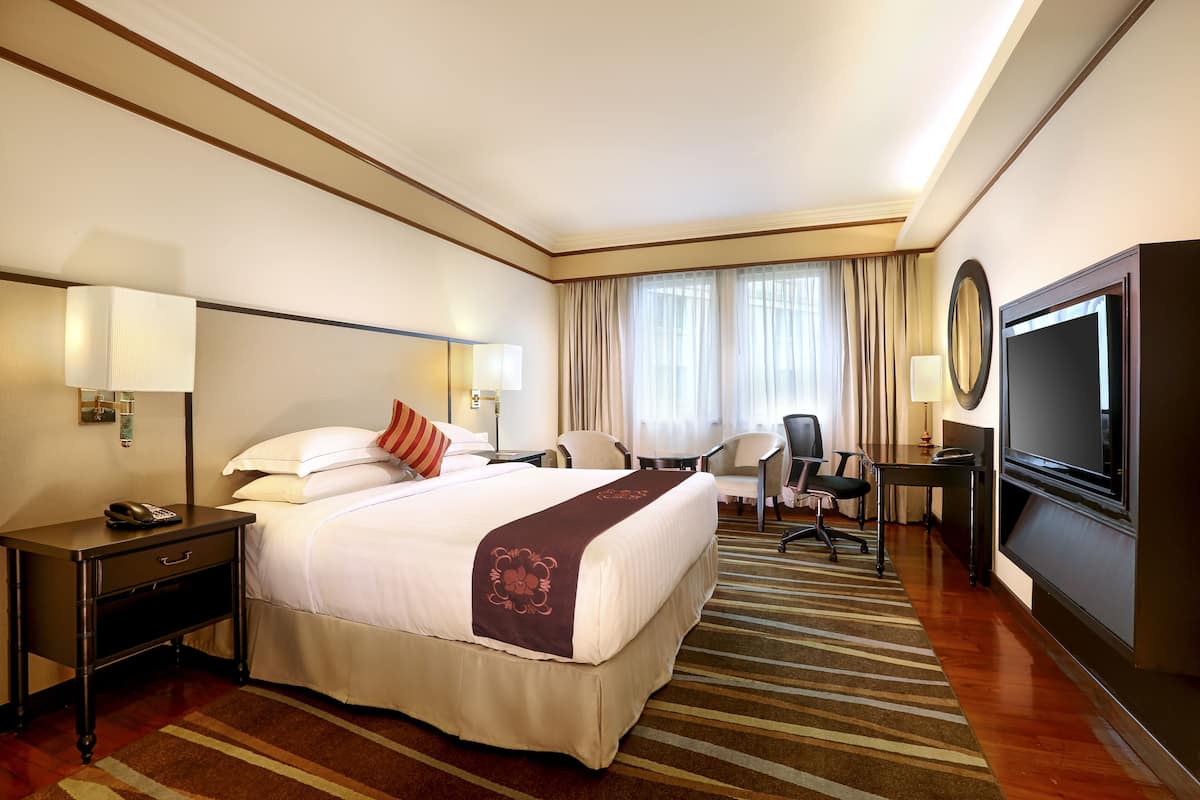 Quarto de hotel com cama grande, mesas de cabeceira, escrivaninha, cadeira, televisão e janela com cortinas.