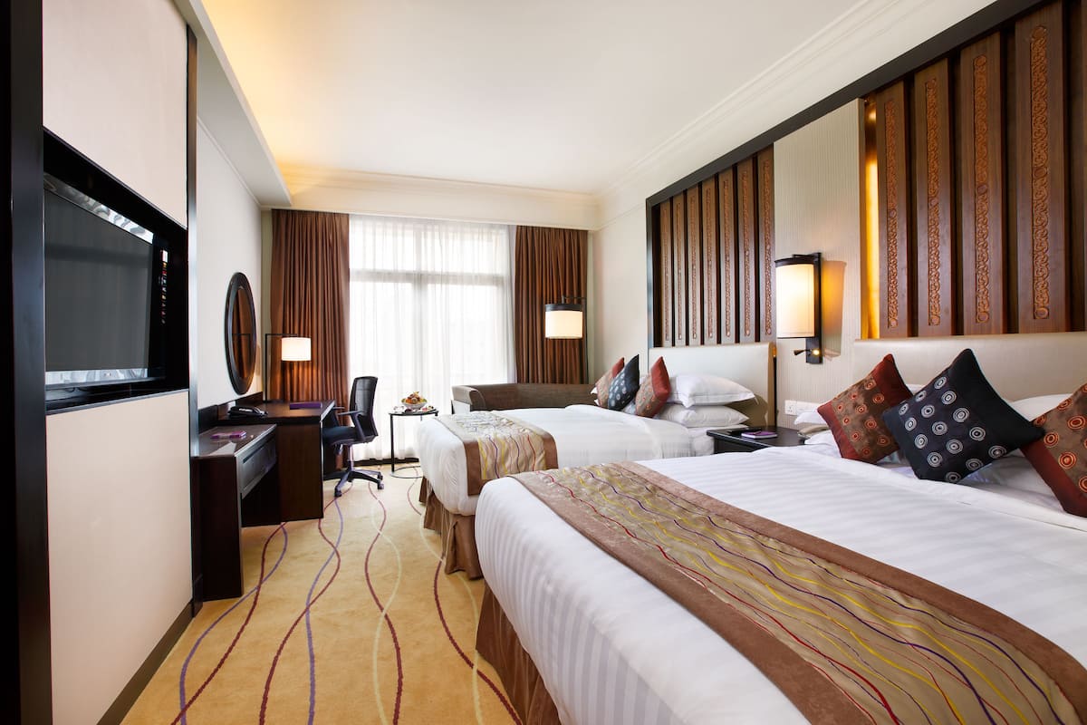 Quarto de hotel com duas camas, uma escrivaninha, uma cadeira, televisão e uma janela grande com cortinas.