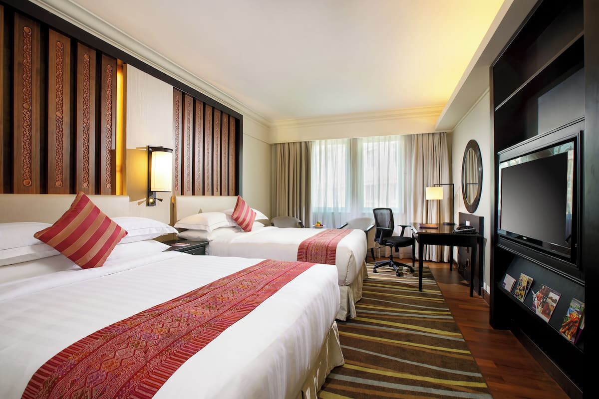 Quarto de hotel com duas camas, uma escrivaninha, televisão e piso carpeteado.