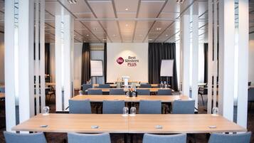 Sala de conferência com uma mesa comprida, várias cadeiras, um quadro branco e uma placa com a inscrição 'Best Western PLUS'.