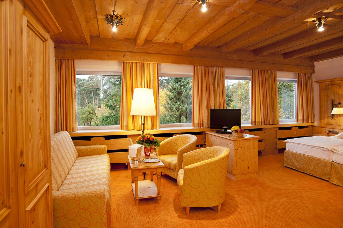Um quarto estilo cabana de madeira, com um sofá, duas poltronas, uma escrivaninha com abajur, uma televisão e uma cama.