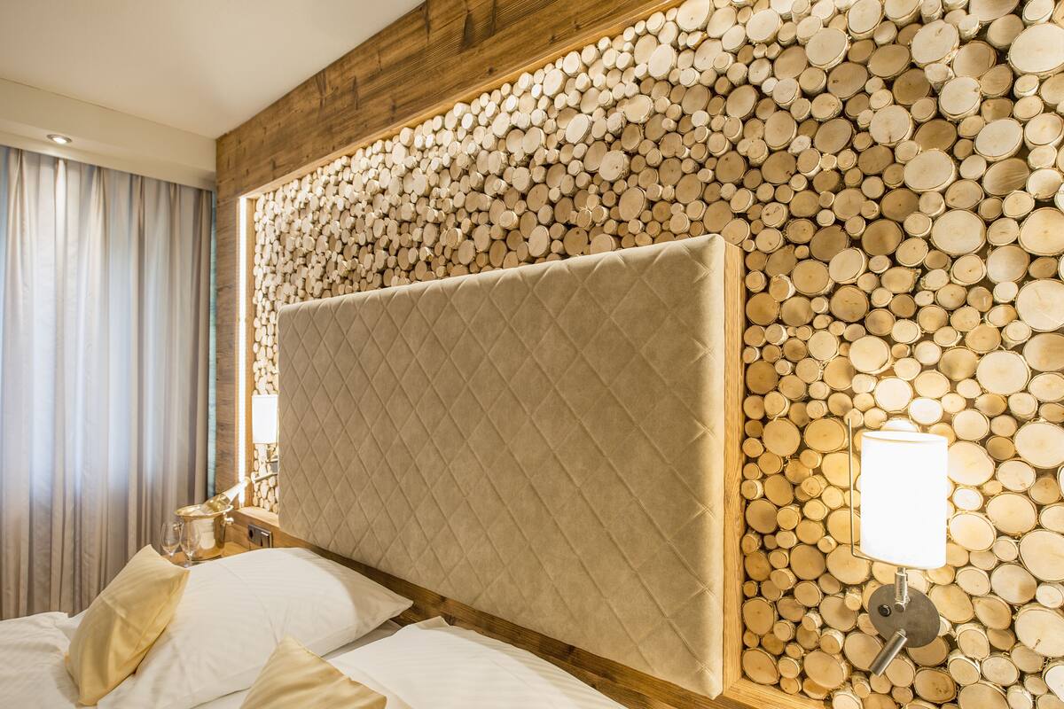 Quarto de hotel com uma cama grande, cabeceira com design acolchoado e parede decorada com toras empilhadas.