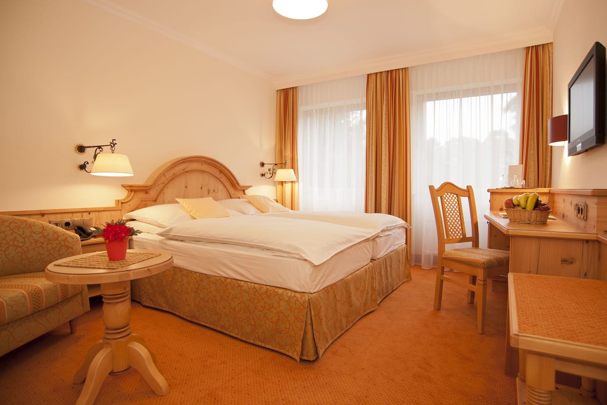 Quarto de hotel com uma cama grande, área de estar com sofá e uma pequena mesa, escrivaninha com cadeira e televisão na parede.