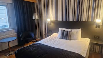 Quarto de hotel com cama, poltrona, mesinha e janela.