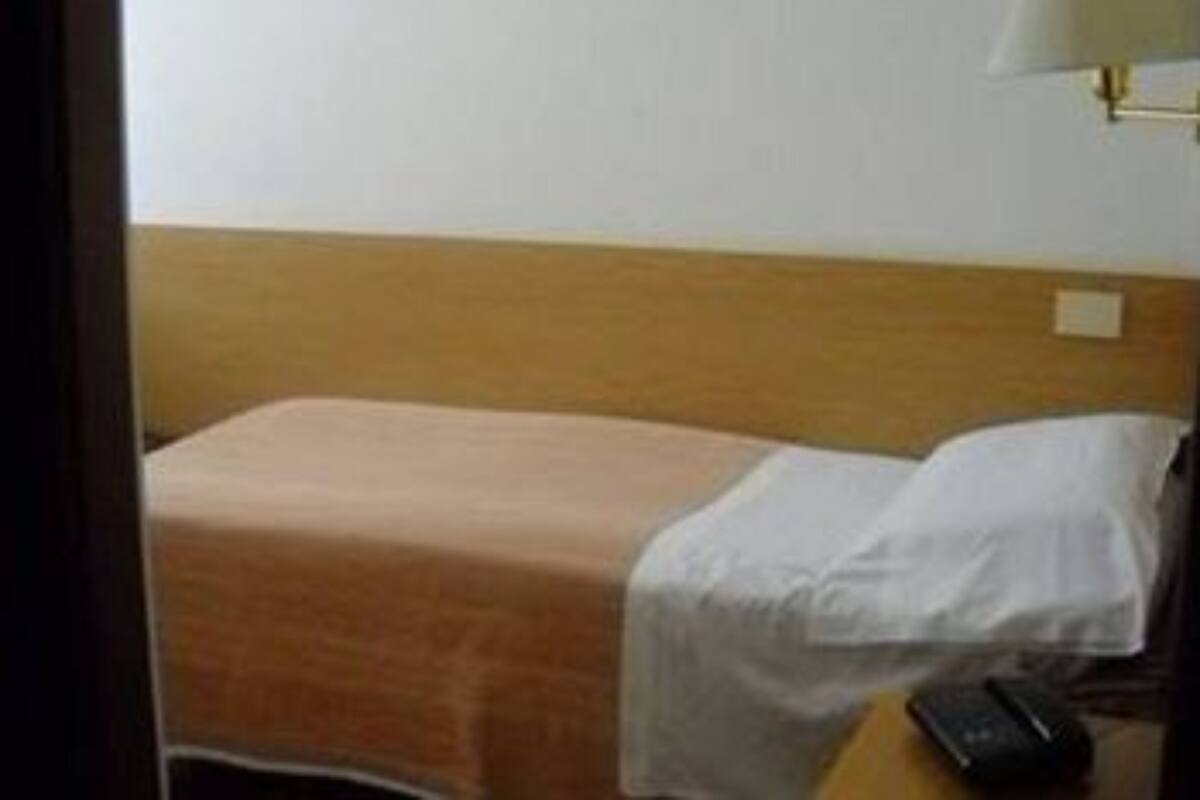 Uma cama de solteiro com cabeceira de madeira, travesseiro branco e mesa de cabeceira com abajur.