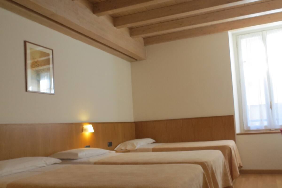 Quarto de hotel com duas camas, vigas de madeira no teto, abajur e janela com cortinas.