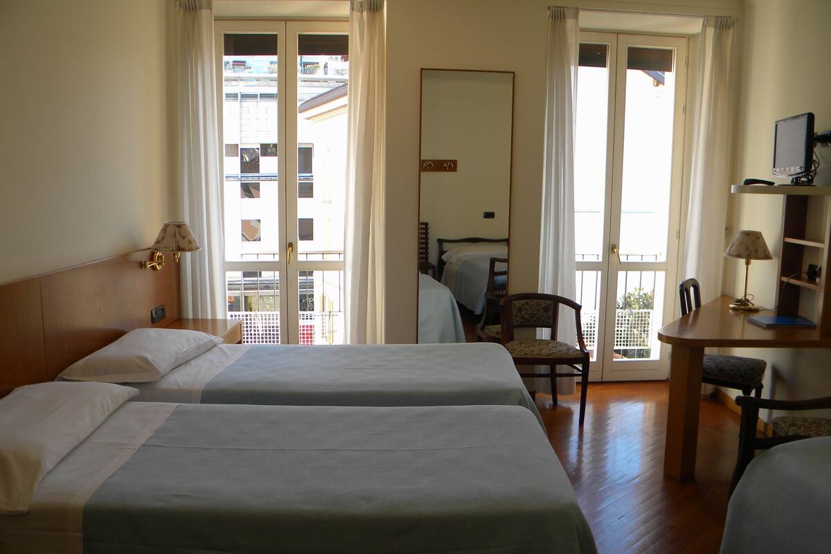 Quarto de hotel com duas camas, uma escrivaninha, uma cadeira e uma televisão.